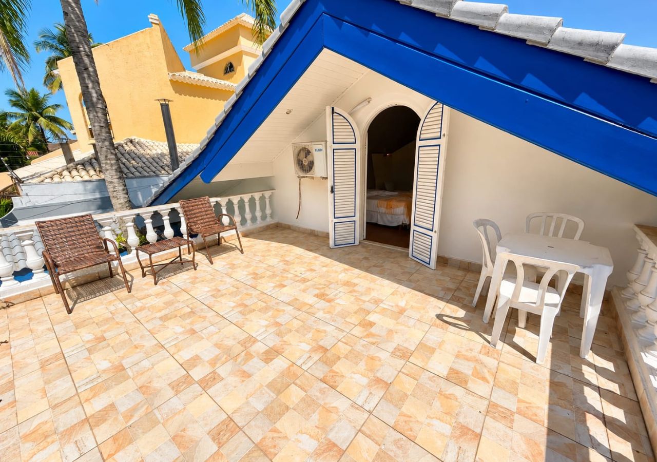 Um pátio ao ar livre banhado pelo sol, com piso de azulejos, uma mesa com cadeiras e um pequeno espaço de estar com um banco.