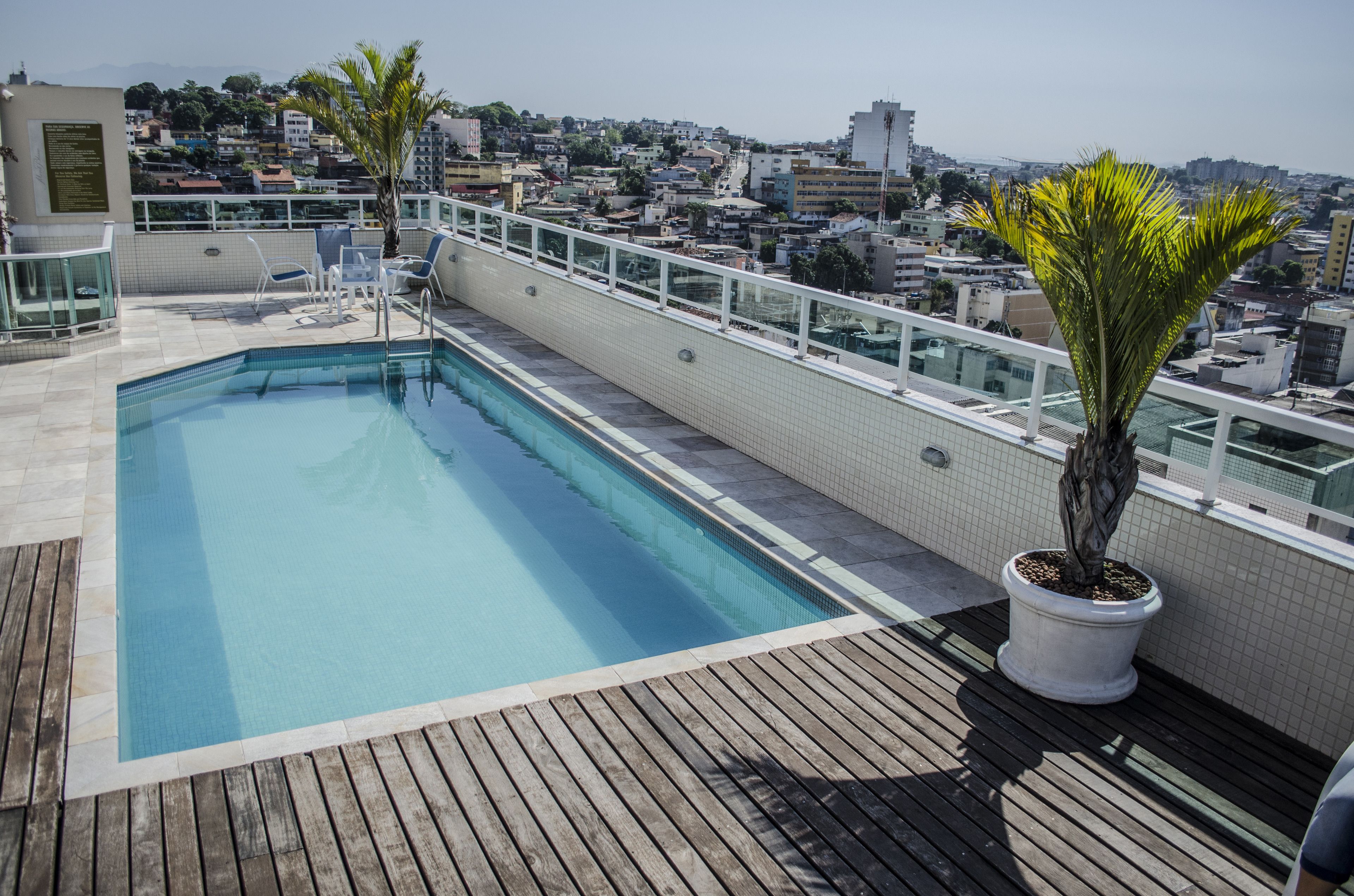 Uma piscina no terraço com deck de madeira, grades brancas e vista para a paisagem urbana.