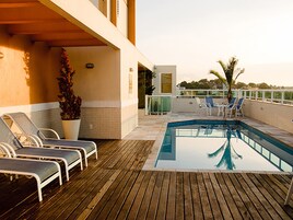 Área de piscina no terraço com espreguiçadeiras, uma piscina pequena e um vaso de planta.