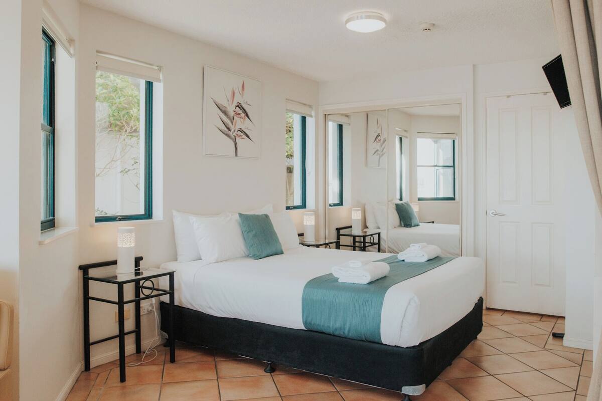 Quarto de hotel com cama, mesas de cabeceira, abajur e espelho.