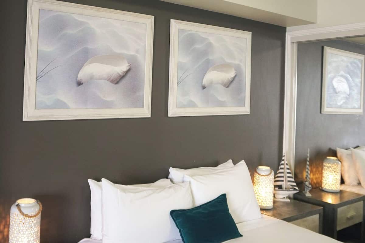 Quarto de hotel com cama, mesas de cabeceira, luminárias decorativas e obras de arte na parede.