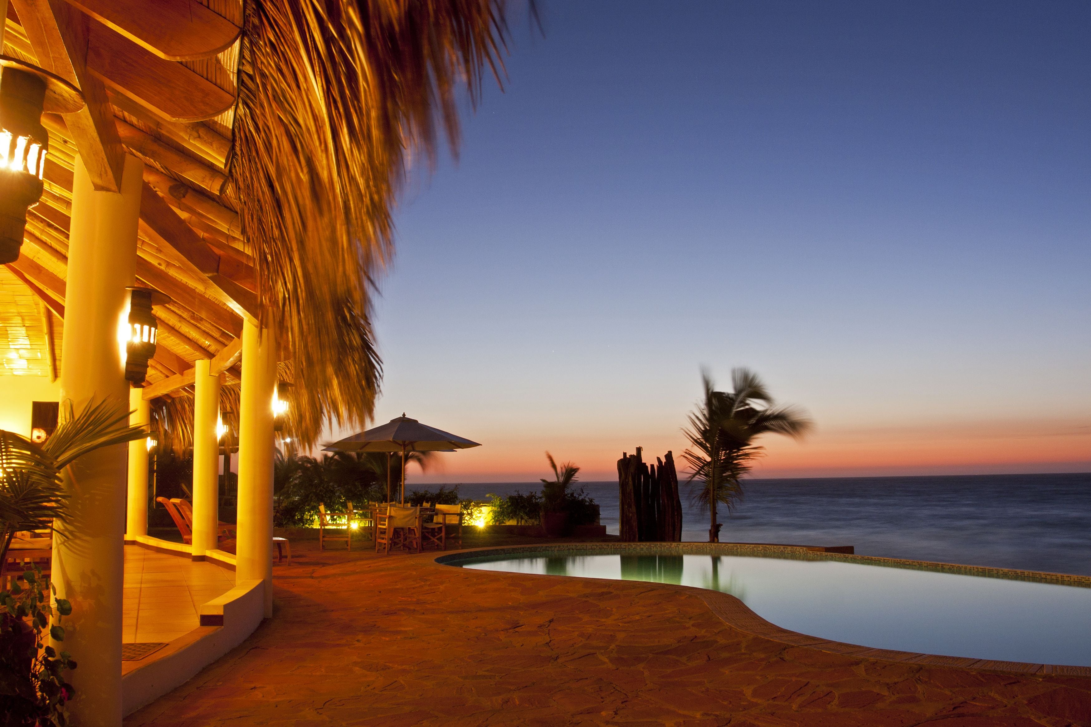 Área da piscina com vista para o oceano ao pôr do sol.