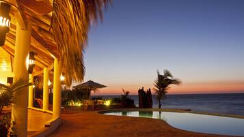 Área da piscina com vista para o oceano ao pôr do sol.