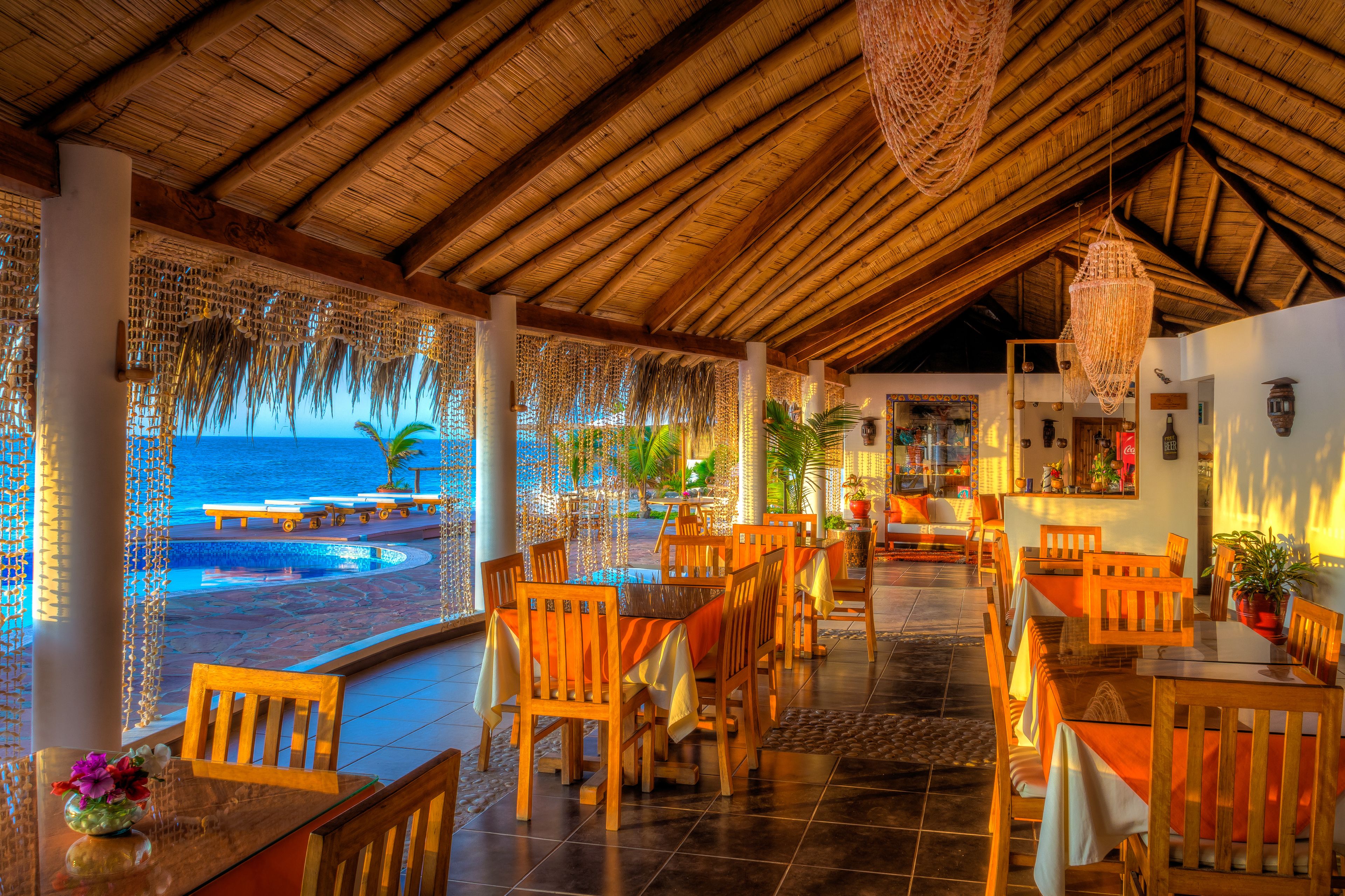 Restaurante com vista para o oceano, mobiliário de madeira e telhado de palha.
