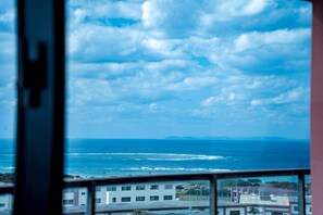 Vista do oceano e da terra ao longe através de uma janela, com edifícios em primeiro plano.