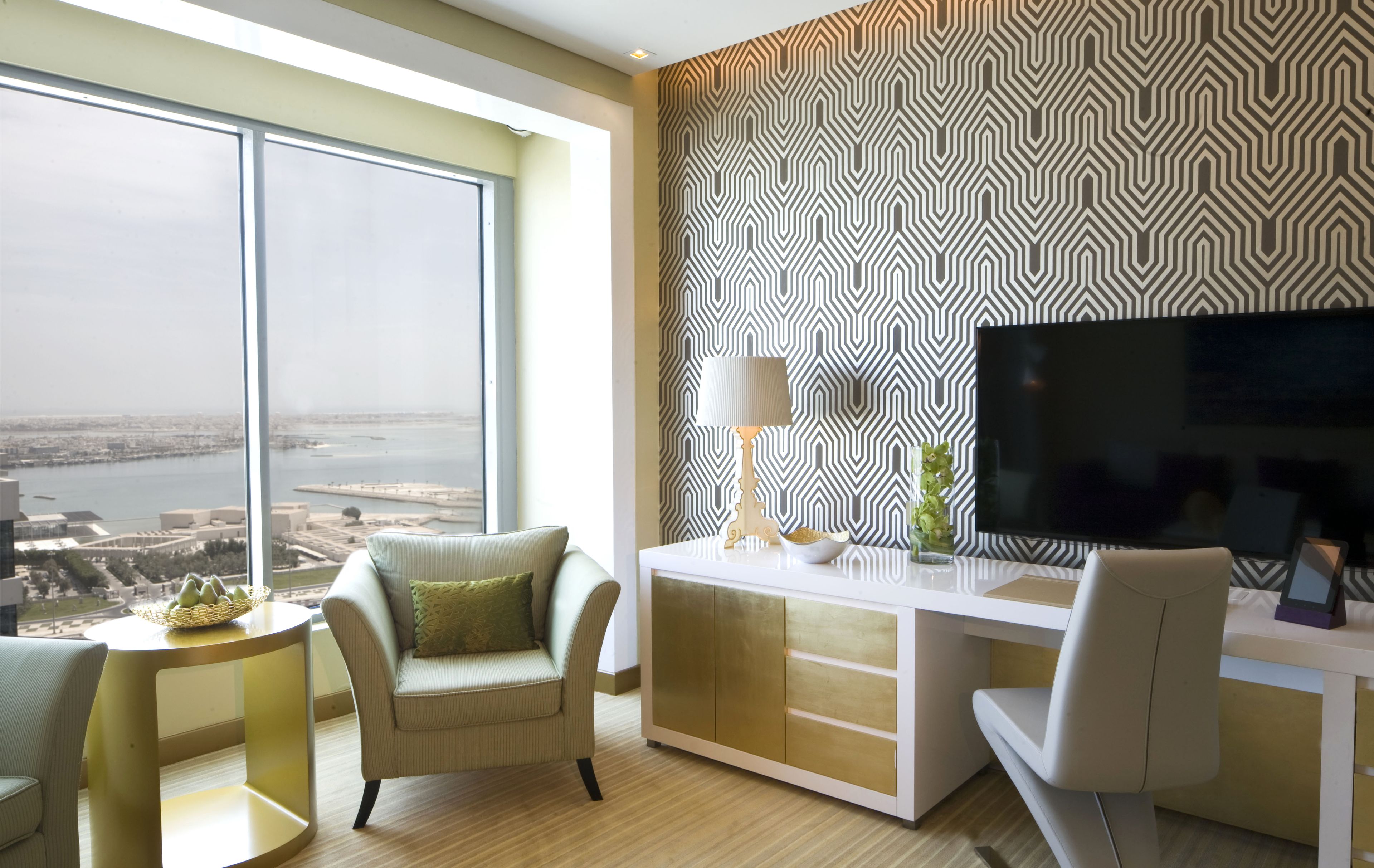 Quarto de hotel moderno com uma janela ampla que oferece vista para a cidade, televisão de tela plana, escrivaninha branca e área de estar confortável.