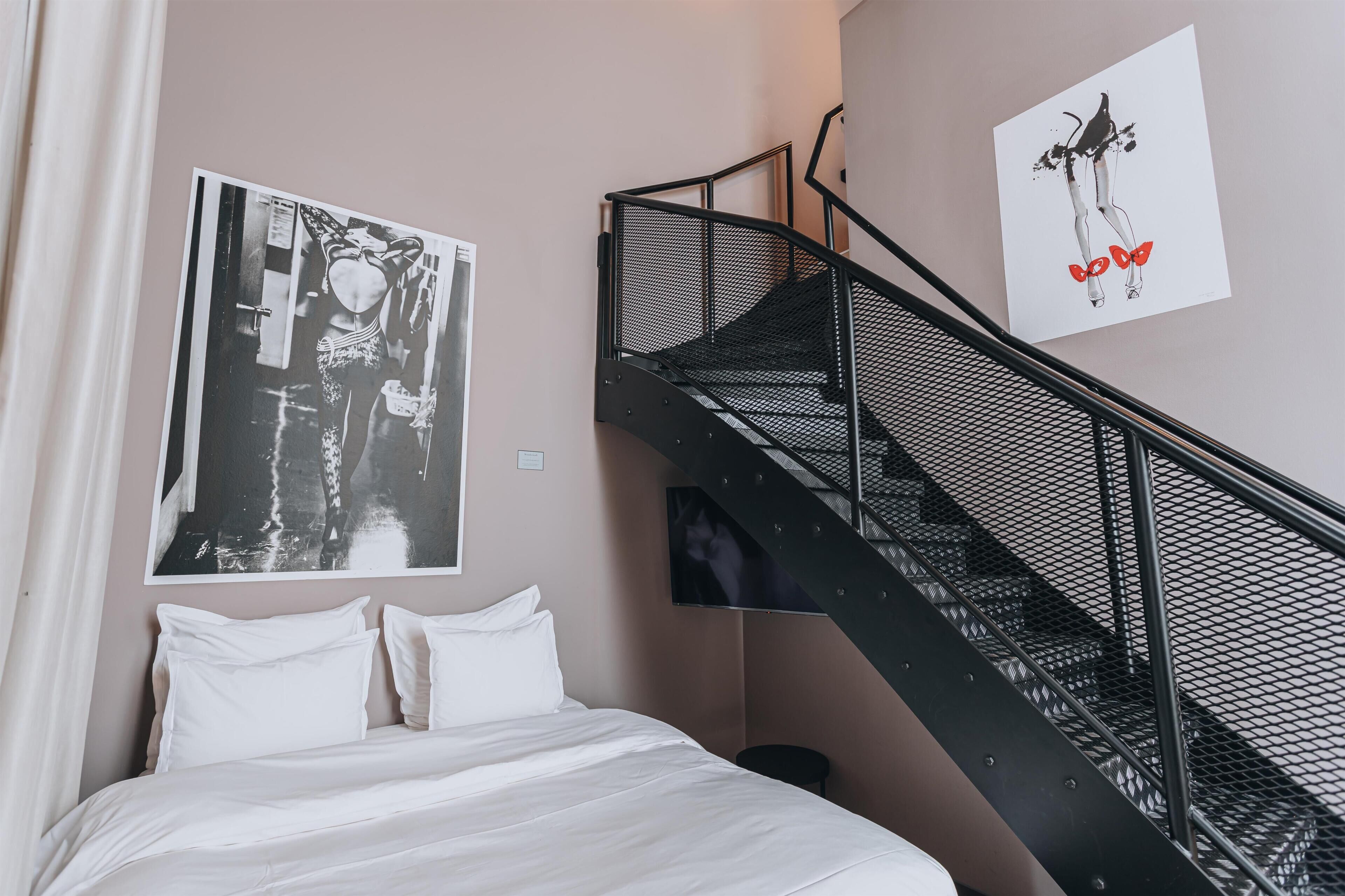 Quarto com cama, escada de metal preto e duas obras de arte penduradas na parede.