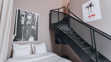 Quarto com cama, escada de metal preto e duas obras de arte penduradas na parede.