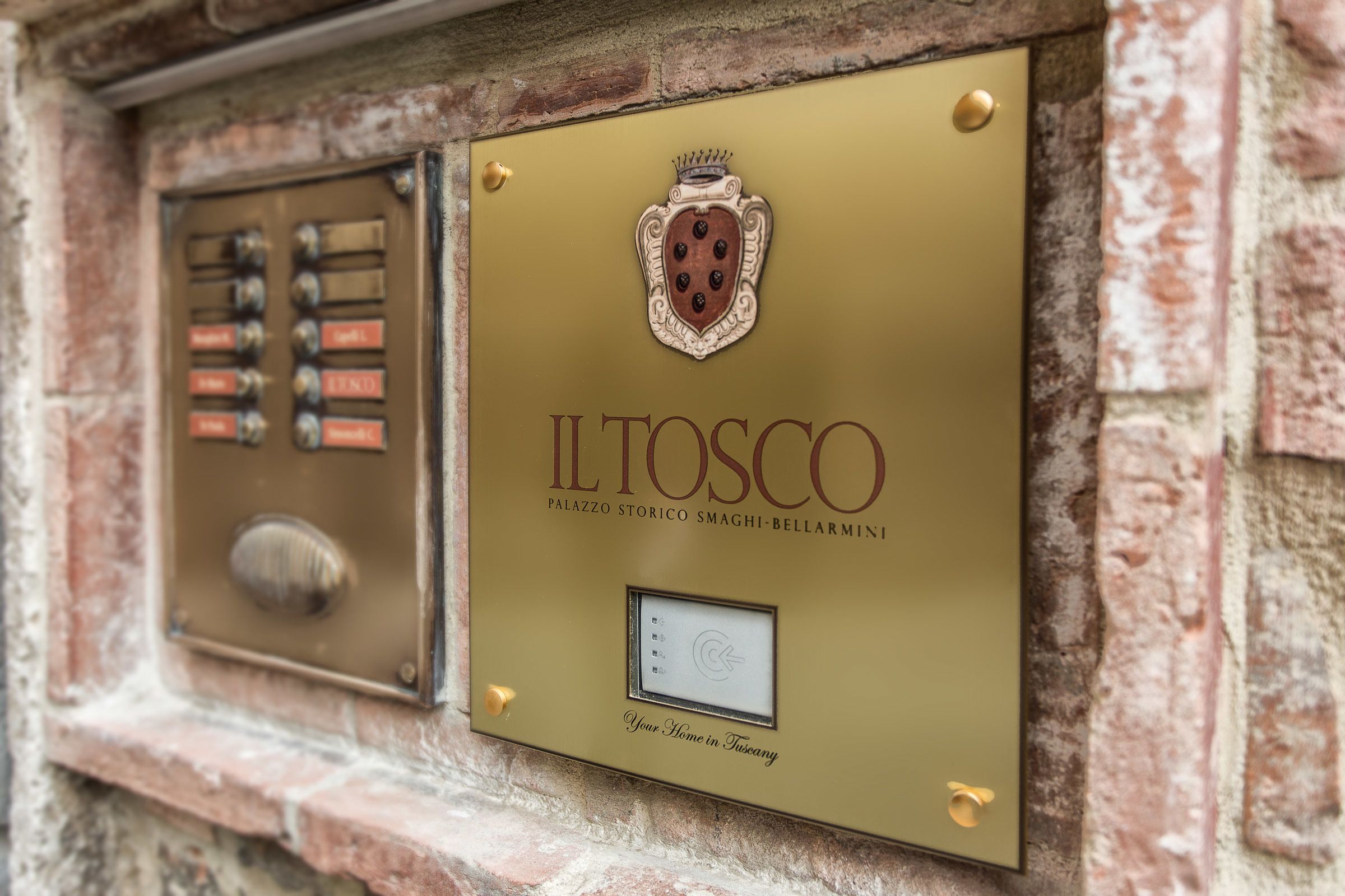 Uma placa com o nome "IL TOSCO" e a frase "Your Home in Tuscany" numa parede de tijolos.