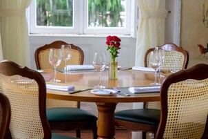 Mesa de jantar posta para seis lugares, cadeiras, um vaso de rosas vermelhas e taças de vinho.
