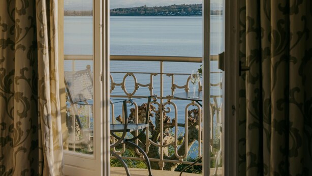 Quarto com cama e varanda com vista para um lago e montanhas.