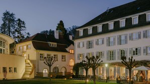 Um edifício grande com uma escadaria central, várias janelas e um jardim bem cuidado com árvores.