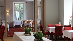 Uma área de refeições com mesas preparadas para o serviço, uma grande janela com vista e um tapete vermelho que leva ao espaço do restaurante.