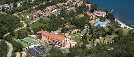 Vista aérea de uma área residencial costeira com casas, piscina e campo esportivo.