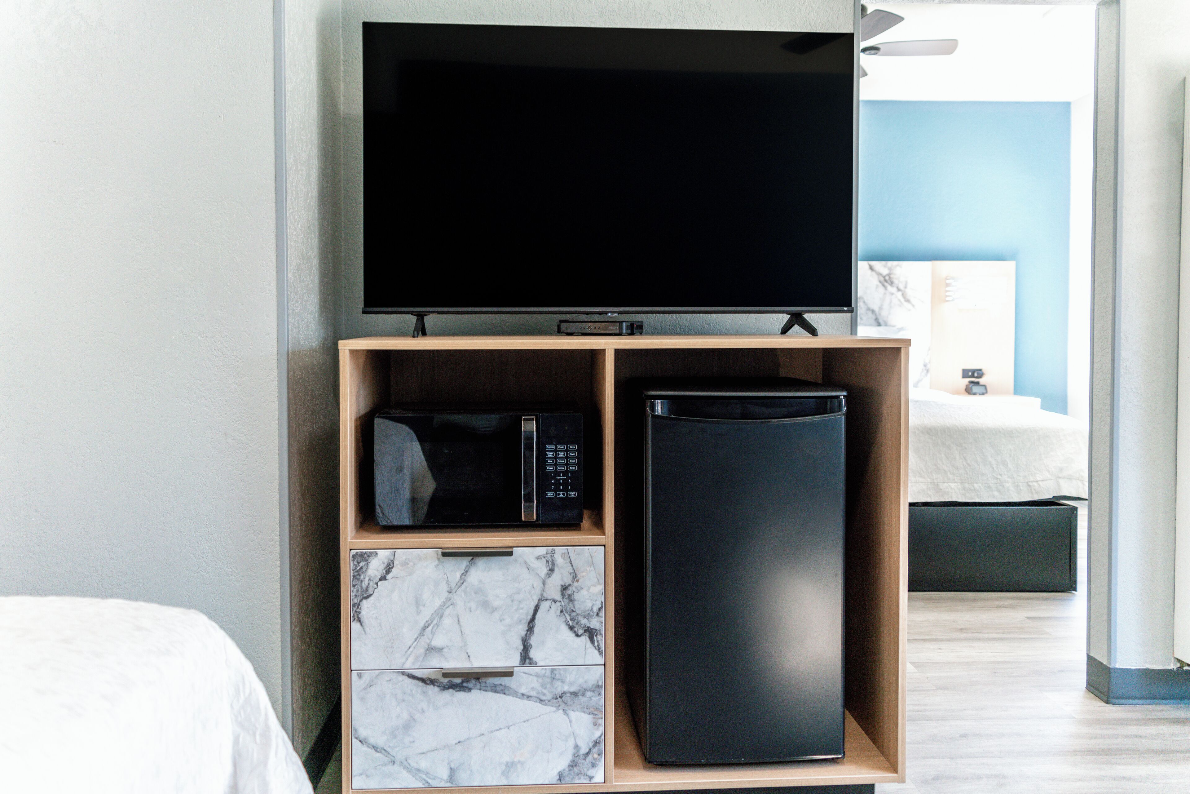 Quarto de hotel com televisão de tela plana em suporte de madeira, micro-ondas e geladeira preta.