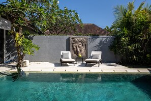Uma piscina com duas espreguiçadeiras e uma estátua de Buda na parede.