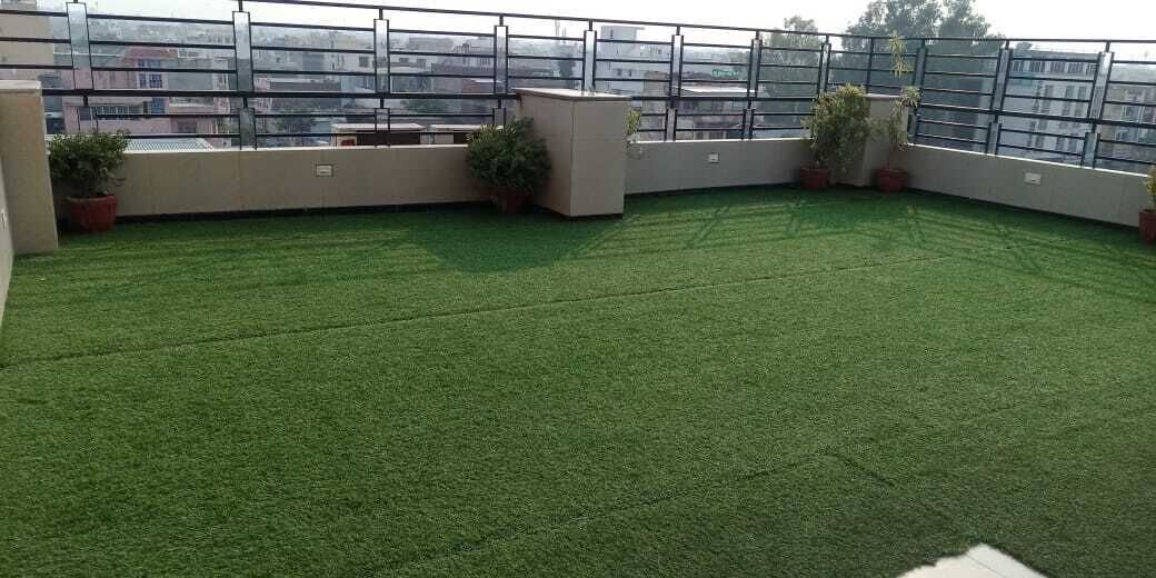 Terraço no telhado com grama artificial, plantas em vasos e vista para a paisagem urbana.