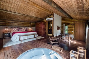 Quarto aconchegante com cama grande, piso de madeira, hidromassagem e área de jantar com cadeiras e mesa.