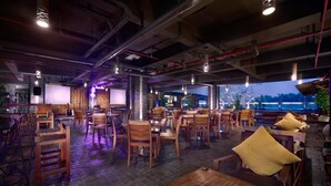 Restaurante com mesas e cadeiras de madeira, área de bar e vista para o exterior.
