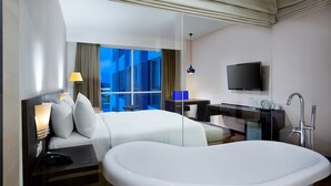 Quarto de hotel moderno com uma cama grande, área de trabalho separada, TV de tela plana, banheira espaçosa e vista para a cidade pela janela.