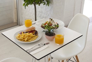 Uma mesa com um hambúrguer, batatas fritas, salada e dois copos de suco de laranja.