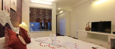 Quarto de hotel com cama, almofadas, televisão e guarda-roupa.