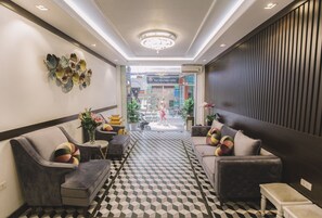 Um lobby moderno com piso xadrez, sofás cinzas e um painel decorativo na parede.