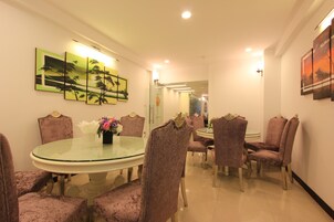 Uma sala de jantar com uma mesa redonda de vidro, rodeada por cadeiras de veludo, obras de arte nas paredes e um espelho refletindo o ambiente.