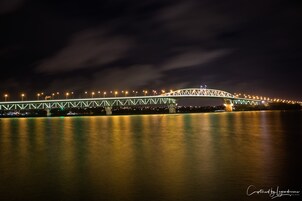 Vista noturna de uma ponte com luzes iluminadas e águas calmas abaixo.