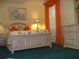 Quarto com cama, mesa de cabeceira, cômoda, abajur e um quadro na parede.