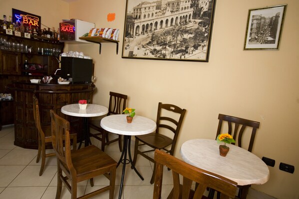 Uma área de bar com cadeiras e mesas de madeira, uma televisão e prateleiras com garrafas e copos.