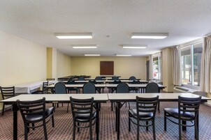 Uma sala de conferências com mesas compridas, cadeiras e uma tela de projeção.