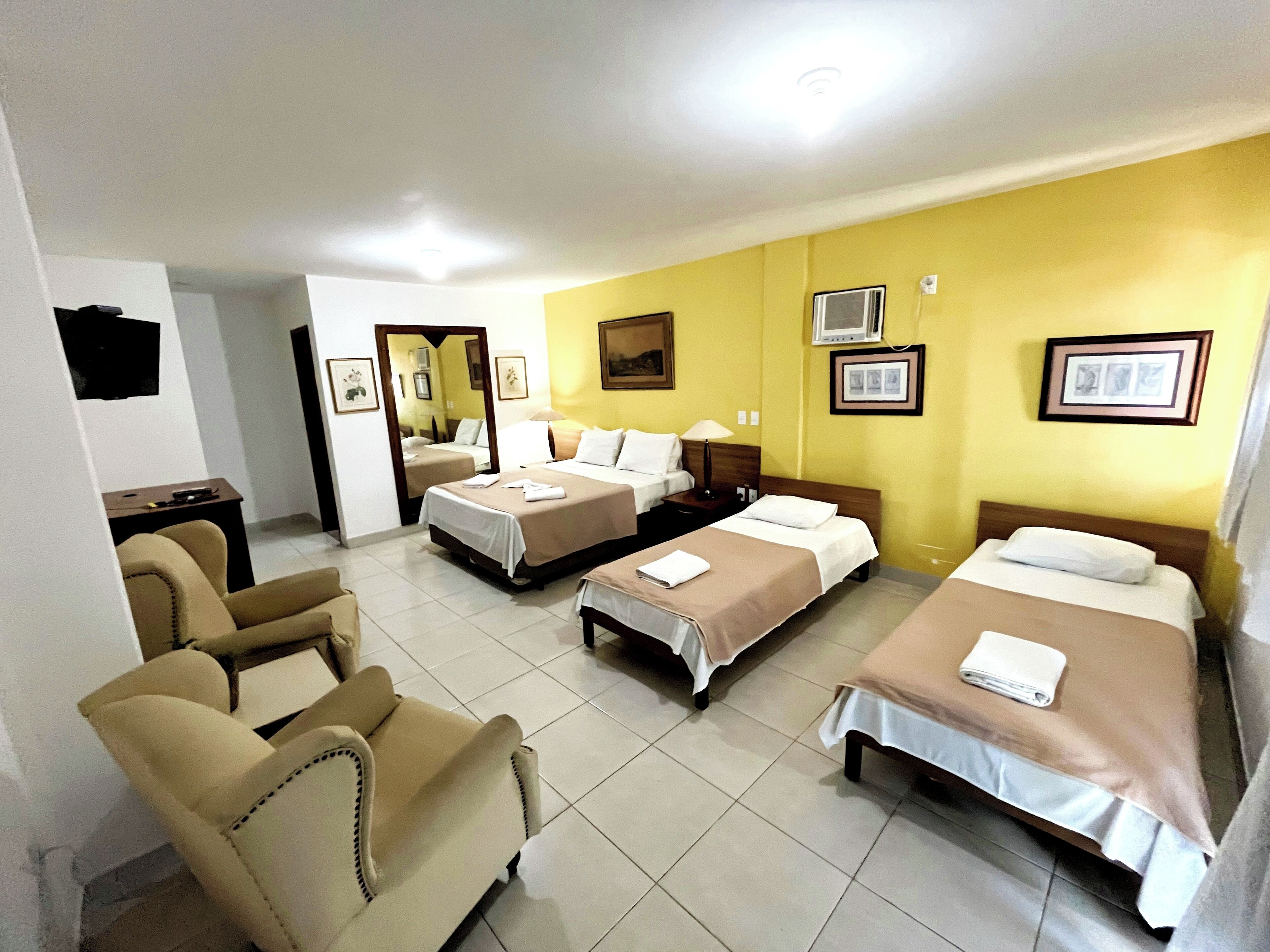 Quarto de hotel com três camas, um sofá e uma televisão.