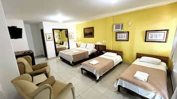 Quarto de hotel com três camas, um sofá e uma televisão.