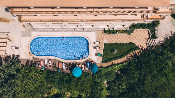 Vista aérea de um hotel com piscina, espreguiçadeiras e um jardim.