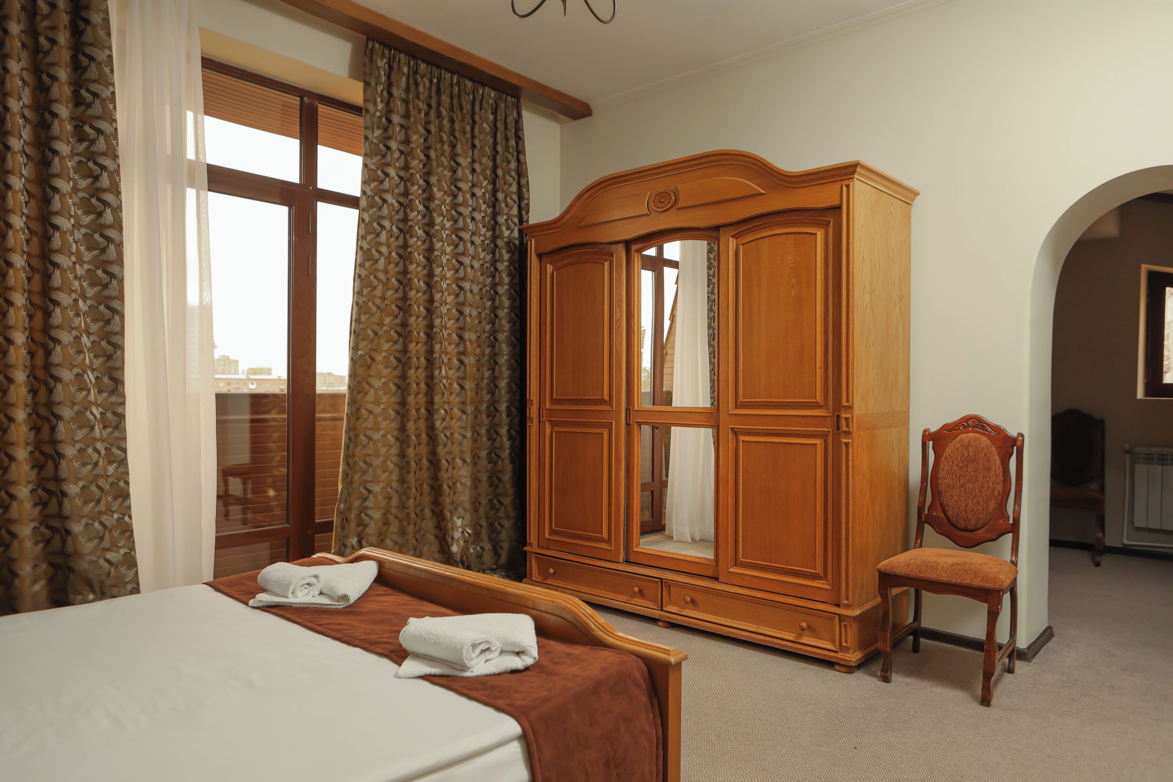 Quarto de hotel com uma cama, um guarda-roupa de madeira, uma cadeira e vista pela janela.