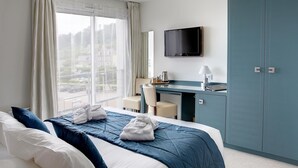 Quarto de hotel com cama, escrivaninha, televisão e guarda-roupa.