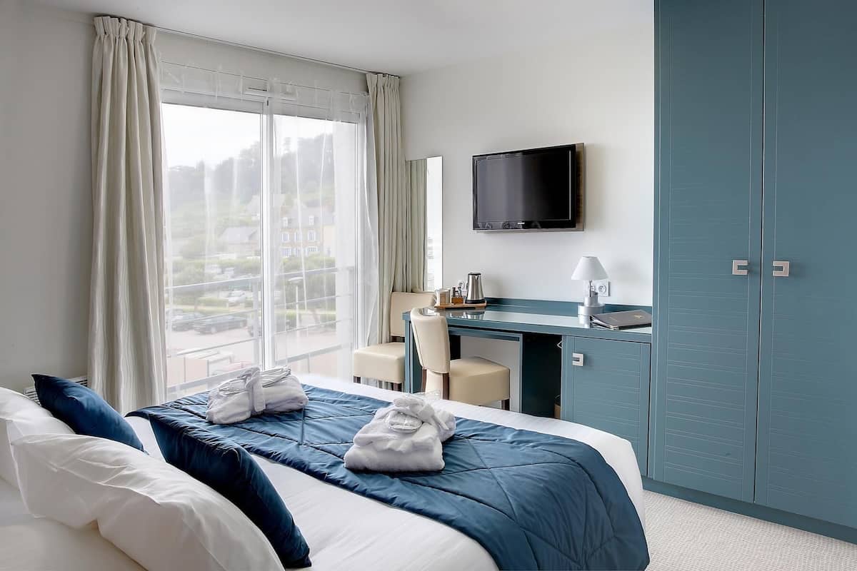 Quarto de hotel com cama, escrivaninha, televisão e guarda-roupa.