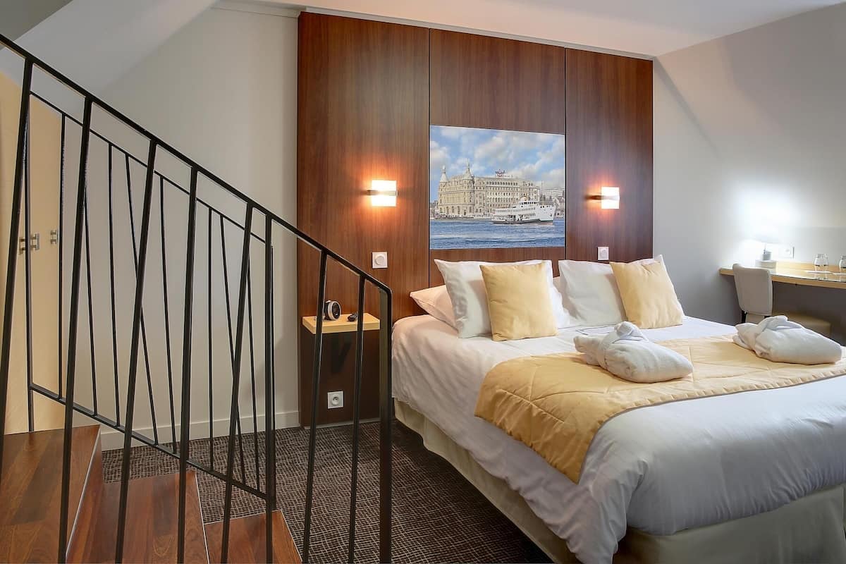 Quarto de hotel com cama, cabeceira de madeira, pintura de um edifício e uma escadaria.