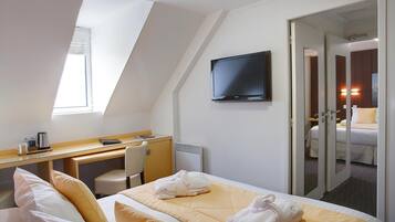 Quarto de hotel com cama, escrivaninha, cadeira, televisão e porta deslizante que dá para outro cômodo.