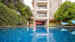 Uma piscina com padrão de azulejos, rodeada por vegetação exuberante e um edifício com varandas.