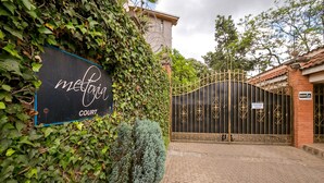 Uma entrada fechada com um letreiro que diz "metziva COURT", cercada por vegetação exuberante.