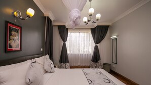Quarto com cama grande, cortinas escuras, lustre e um quadro na parede.