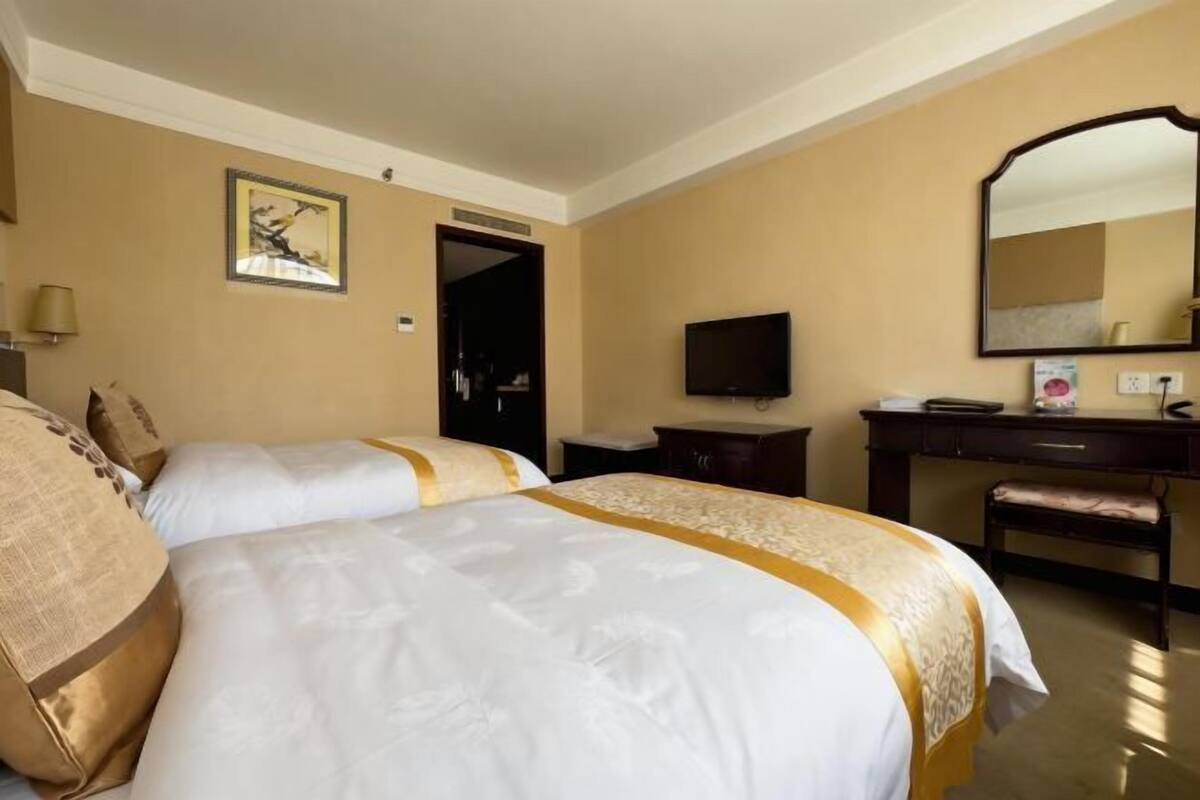 Quarto de hotel com duas camas, televisão, escrivaninha e espelho.