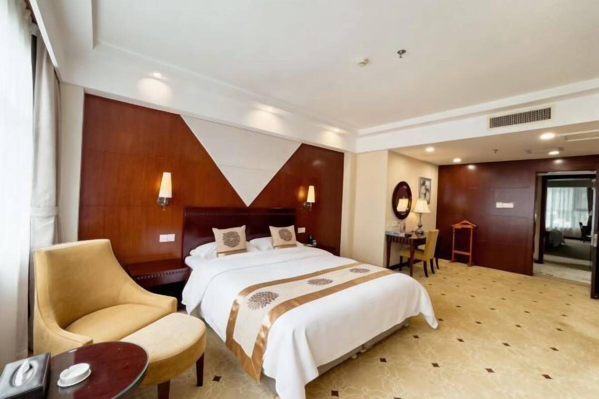 Quarto de hotel com cama, cadeira, escrivaninha e espelho.