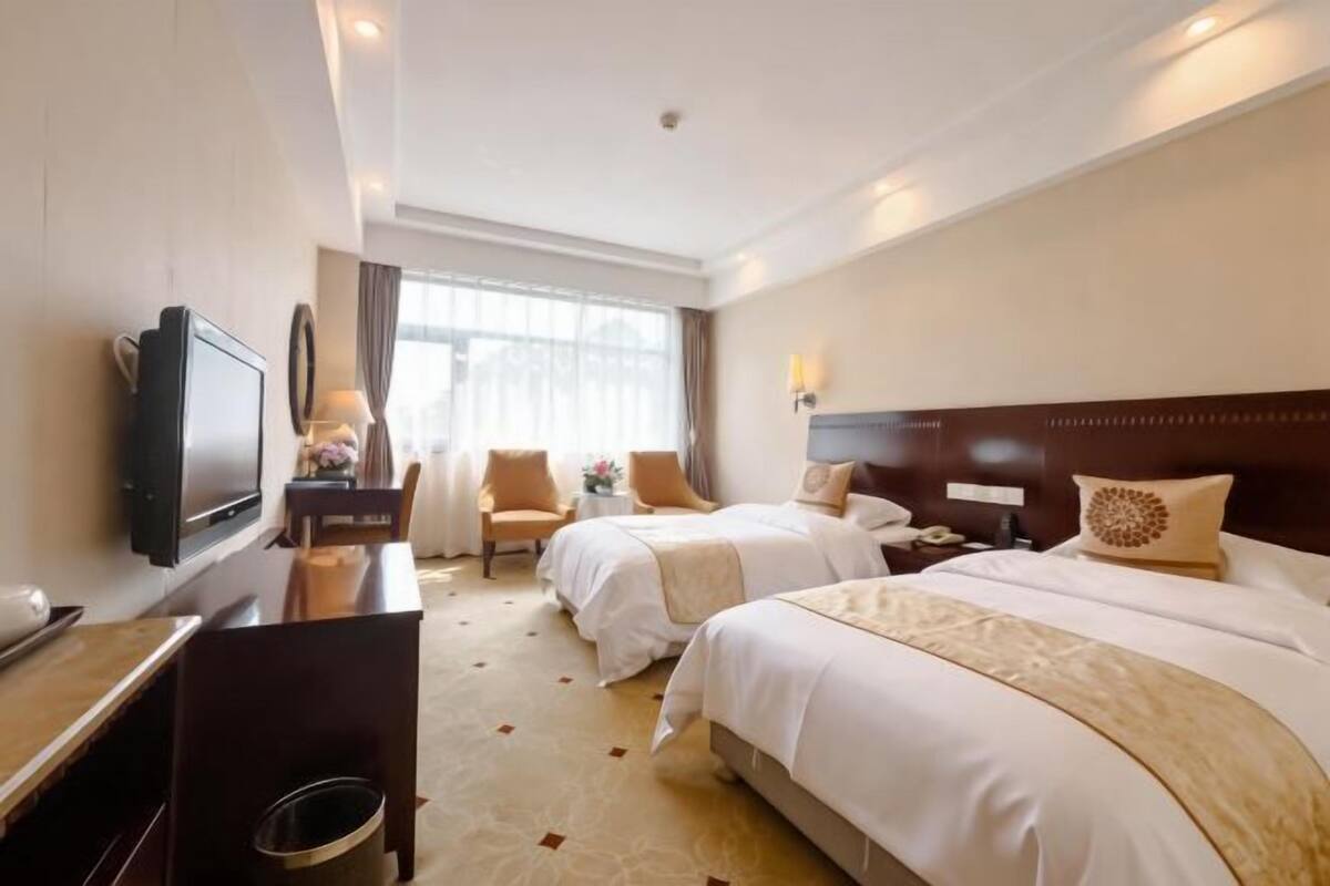 Quarto de hotel com duas camas, televisão, escrivaninha e janela com cortinas.