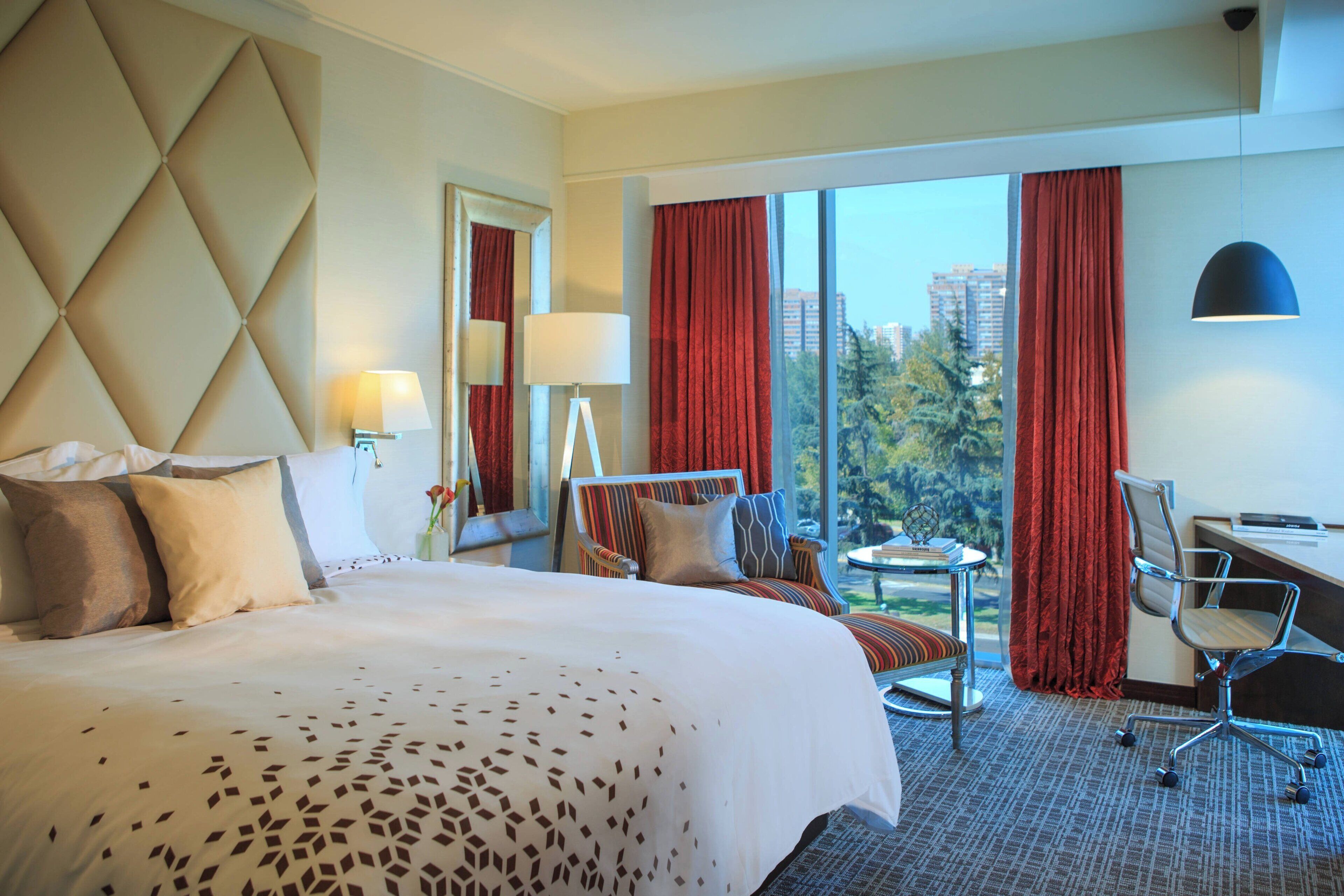 Quarto de hotel com uma cama grande, uma escrivaninha, uma cadeira e vista para a cidade.