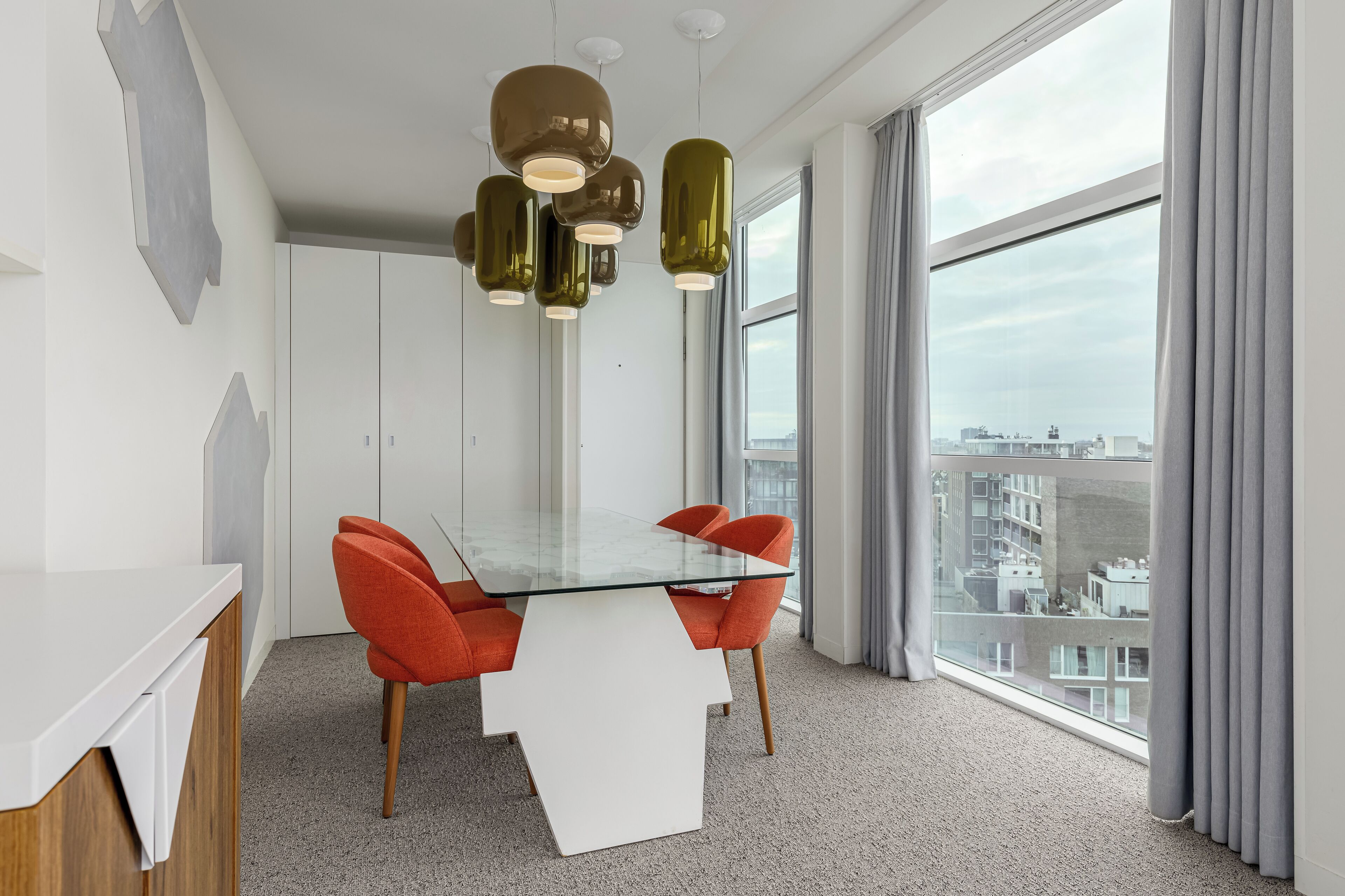 Uma sala de conferências moderna com uma mesa de vidro, cadeiras vermelhas e vista para a cidade.