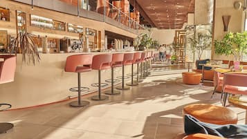 Uma área de bar moderna com banquetas altas, balcão e plantas em vasos.