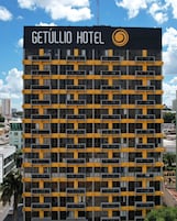 Um hotel imponente com fachada amarela e preta marcante, várias varandas e o nome do hotel em destaque no topo.